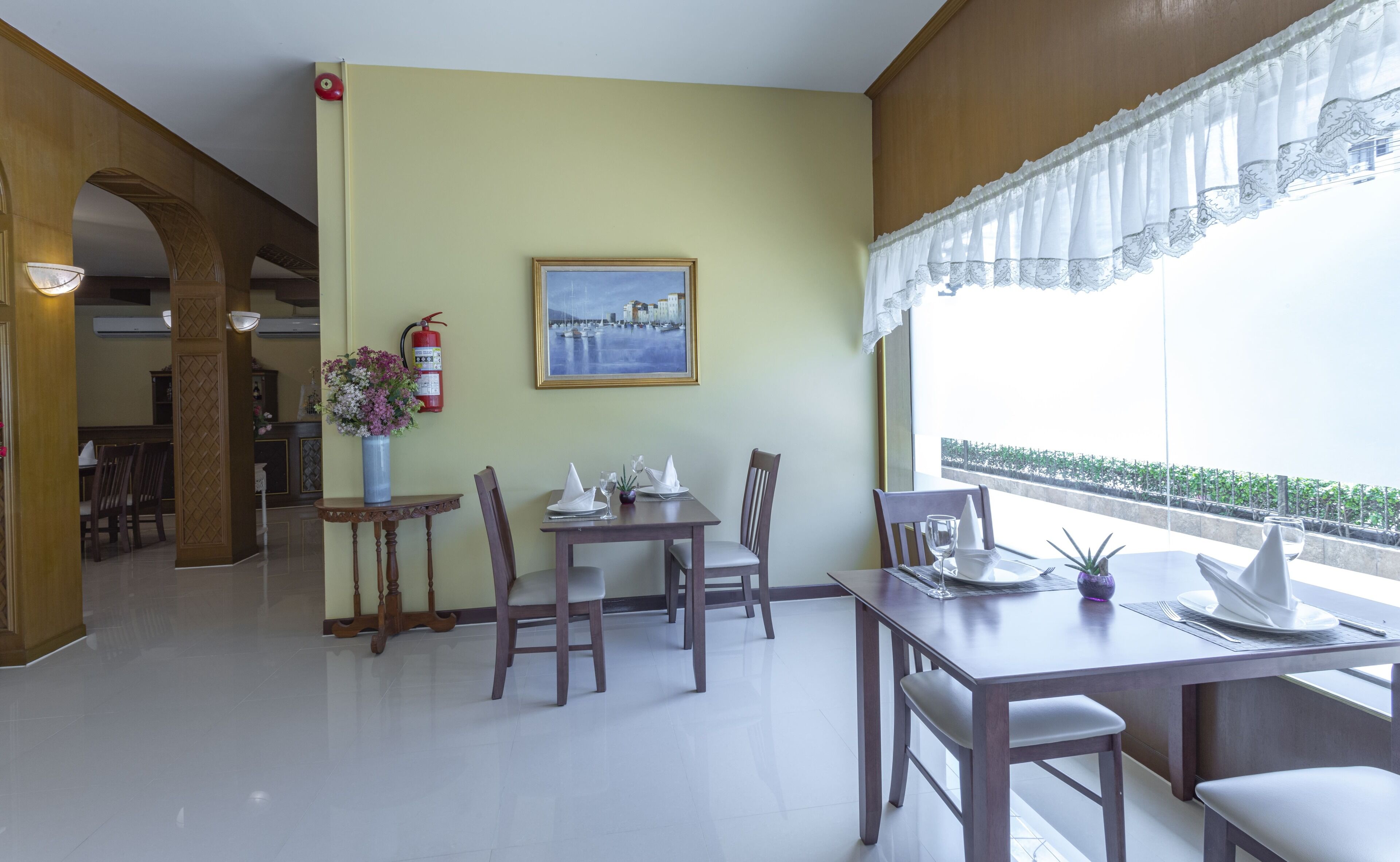 Uma área de refeições com uma mesa posta para dois, um vaso com flores e um extintor de incêndio na parede.