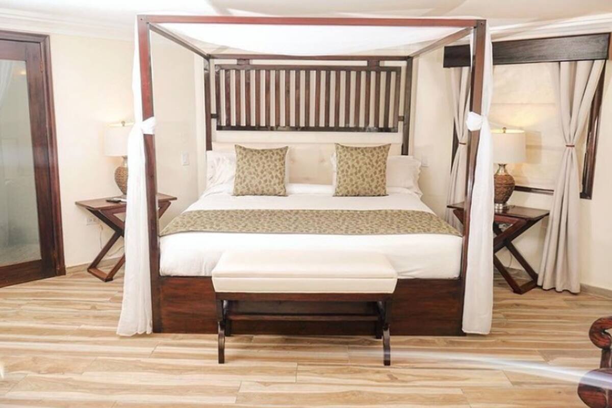 Uma cama de dossel com cortinas, duas mesas de cabeceira e um banquinho.