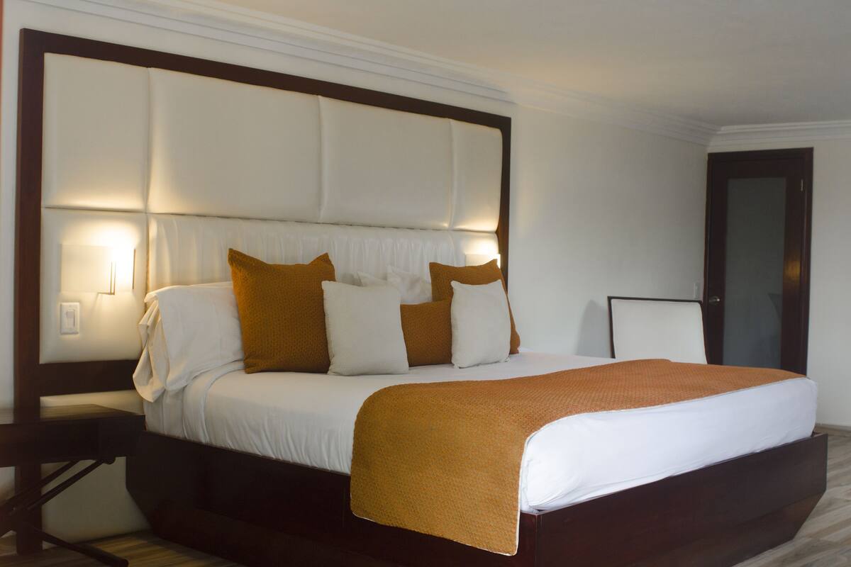 Quarto de hotel com uma cama grande, roupa de cama branca e cabeceira marrom.