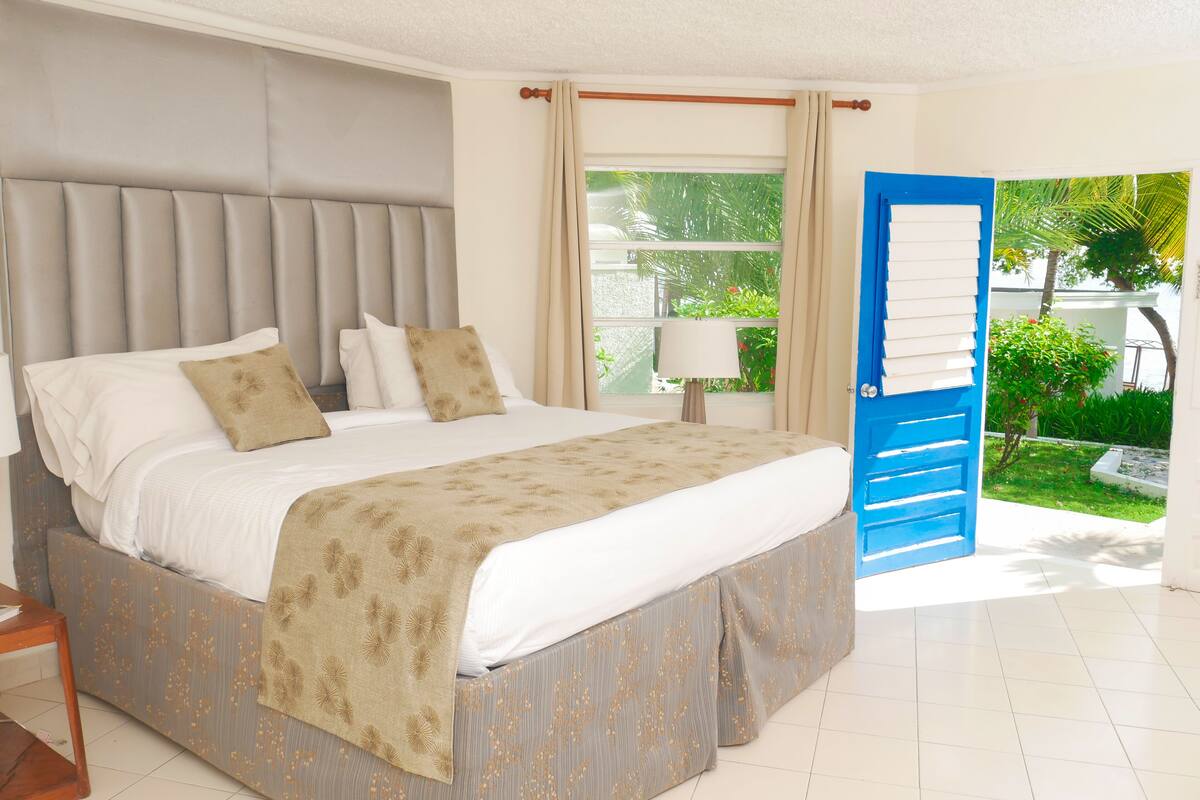 Quarto com uma cama grande, mesa de cabeceira, janela com cortinas e vista para o verde lá fora.