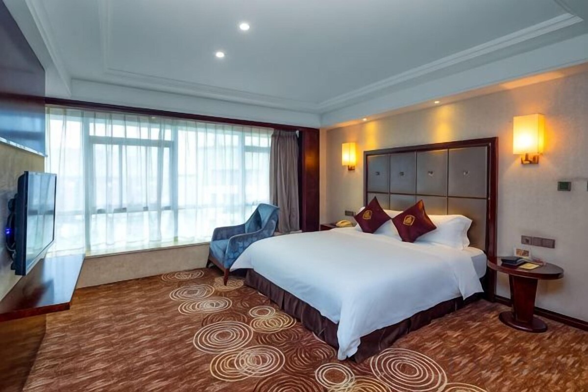 Quarto de hotel com uma cama grande, televisão, escrivaninha e janela com cortinas.