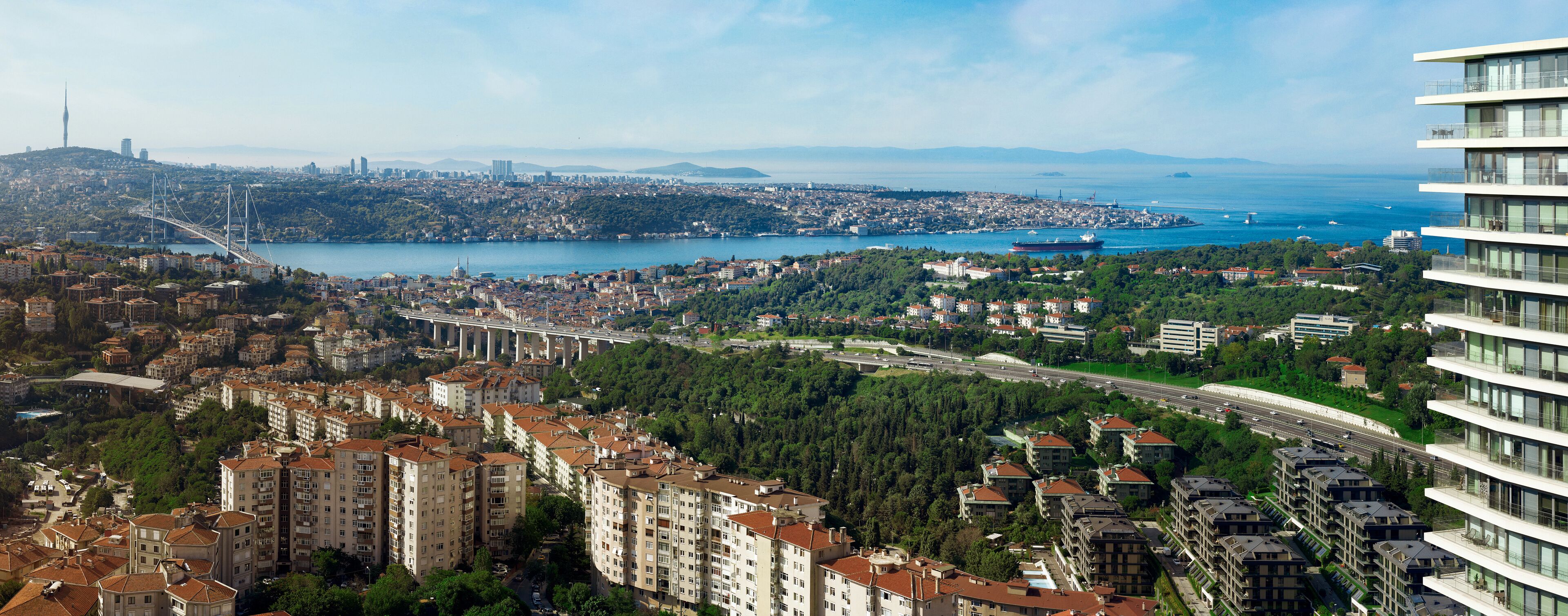 Um hotel de grande porte com vários andares, vista para o horizonte costeiro e uma ponte ao fundo.