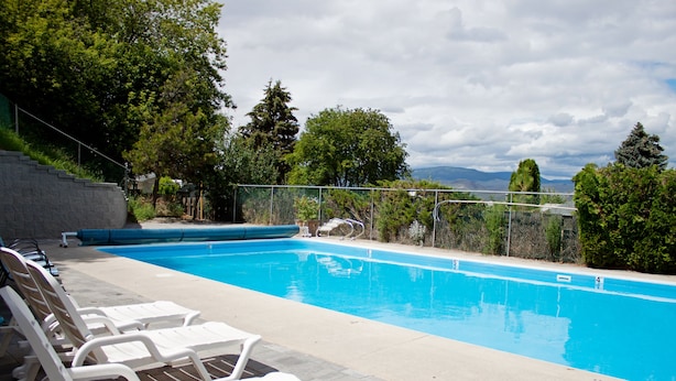 Piscina com espreguiçadeiras brancas e um muro de pedra.