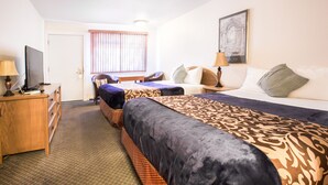 Quarto de hotel com duas camas, uma escrivaninha com televisão, uma cadeira e janela com persianas.