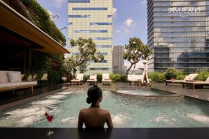 Uma área de piscina no terraço com espreguiçadeiras, um garçom e vista para o horizonte da cidade.