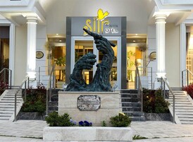 A entrada de um hotel com uma escultura de bronze proeminente de duas figuras, uma placa sobre a entrada e uma escadaria que leva à porta.