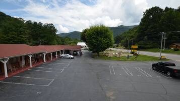 Um motel com teto vermelho, estacionamento e montanhas ao fundo.