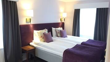 Quarto de hotel com uma cama grande, duas mesinhas de cabeceira e duas luminárias fixadas na parede.