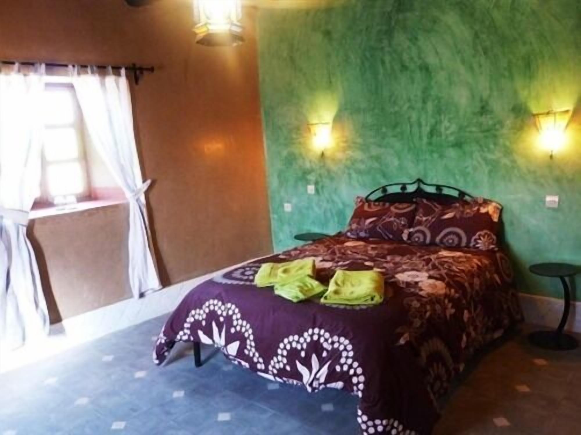 Quarto com cama, duas luminárias na parede, janela com cortinas e uma mesinha.