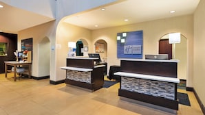 Uma área de recepção de hotel moderna, com dois balcões de atendimento, um espaço para café e uma placa visível da Holiday Inn Express.