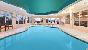Piscina interior com paredes de vidro transparente, cadeiras de descanso e vista para o exterior.