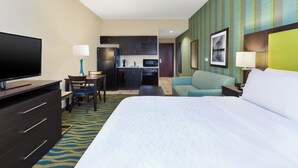 Quarto de hotel com cama, escrivaninha com cadeira, televisão, cozinha compacta e banheiro.