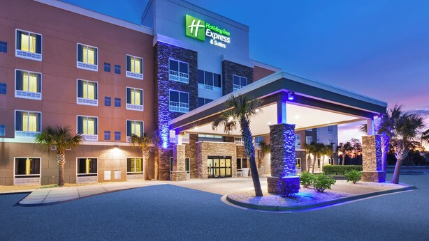 Edifício Holiday Inn Express & Suites com fachada moderna, várias janelas e área de entrada coberta com palmeiras.