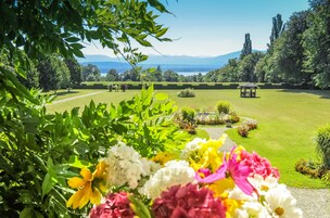 Um jardim exuberante com um gazebo, gramados bem cuidados e uma vista distante das montanhas.