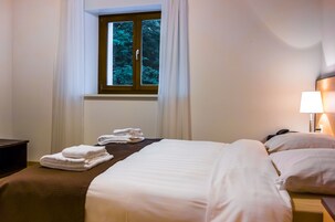 Quarto de hotel com cama, mesa de cabeceira, luminária e janela com cortinas.