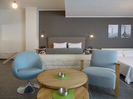 Quarto de hotel com uma cama, duas cadeiras, uma mesinha e uma mesa de cabeceira com abajur.