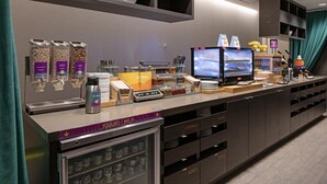 Uma estação de pequeno-almoço de serviço, com dispensadores de iogurte/leite, uma máquina de café e um ecrã digital.