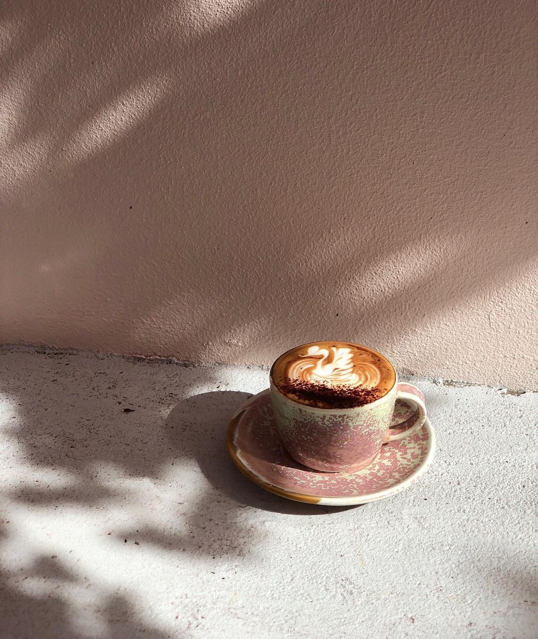 Uma chávena de cerâmica com arte de latte num pires, com uma parede texturizada ao fundo.