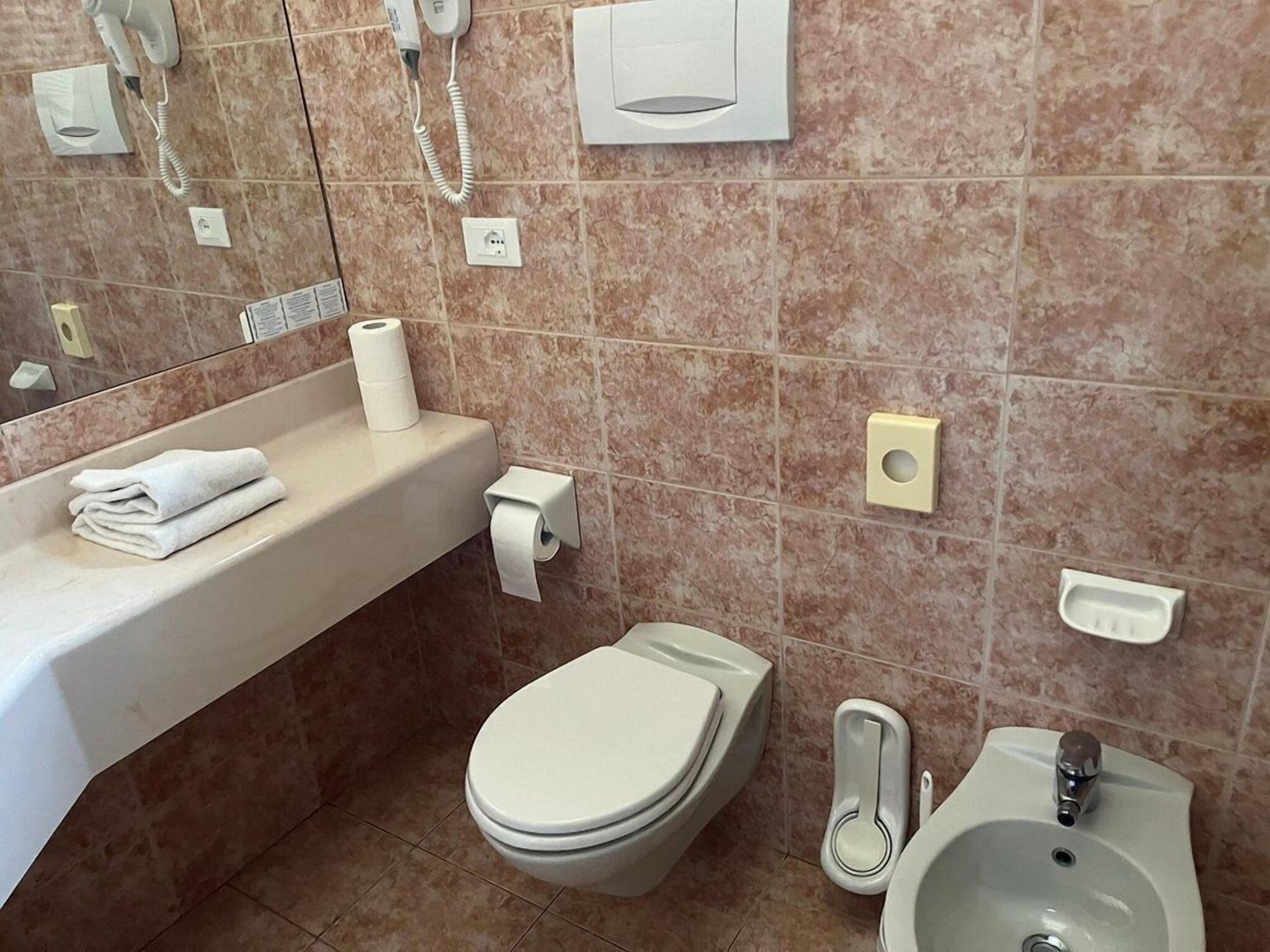 Casa de banho com sanita, bidé, lavatório e suporte para toalhas.