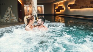Um casal em uma banheira de hidromassagem com um painel de mosaicos e revestimento de madeira ao fundo.