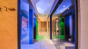 Corredor moderno de hotel com portas de vidro, piso ladrilhado e teto com iluminação embutida.