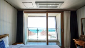 Quarto de hotel com cama, mesa de cabeceira de madeira, escrivaninha com cadeira e uma grande porta de vidro deslizante que dá para uma varanda com vista para o oceano.