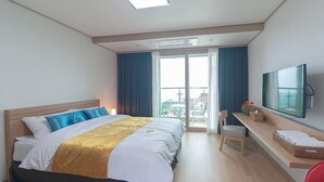 Quarto de hotel com cama, escrivaninha, cadeira, televisão e varanda com vista.
