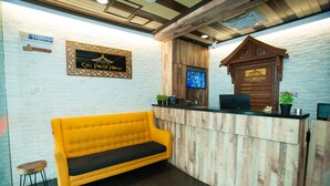 Uma área de recepção com um balcão de madeira, um sofá amarelo e uma tela de TV.