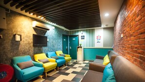 Um hall com piso xadrez, poltronas azuis e amarelas, um sofá marrom e uma parede de tijolos.