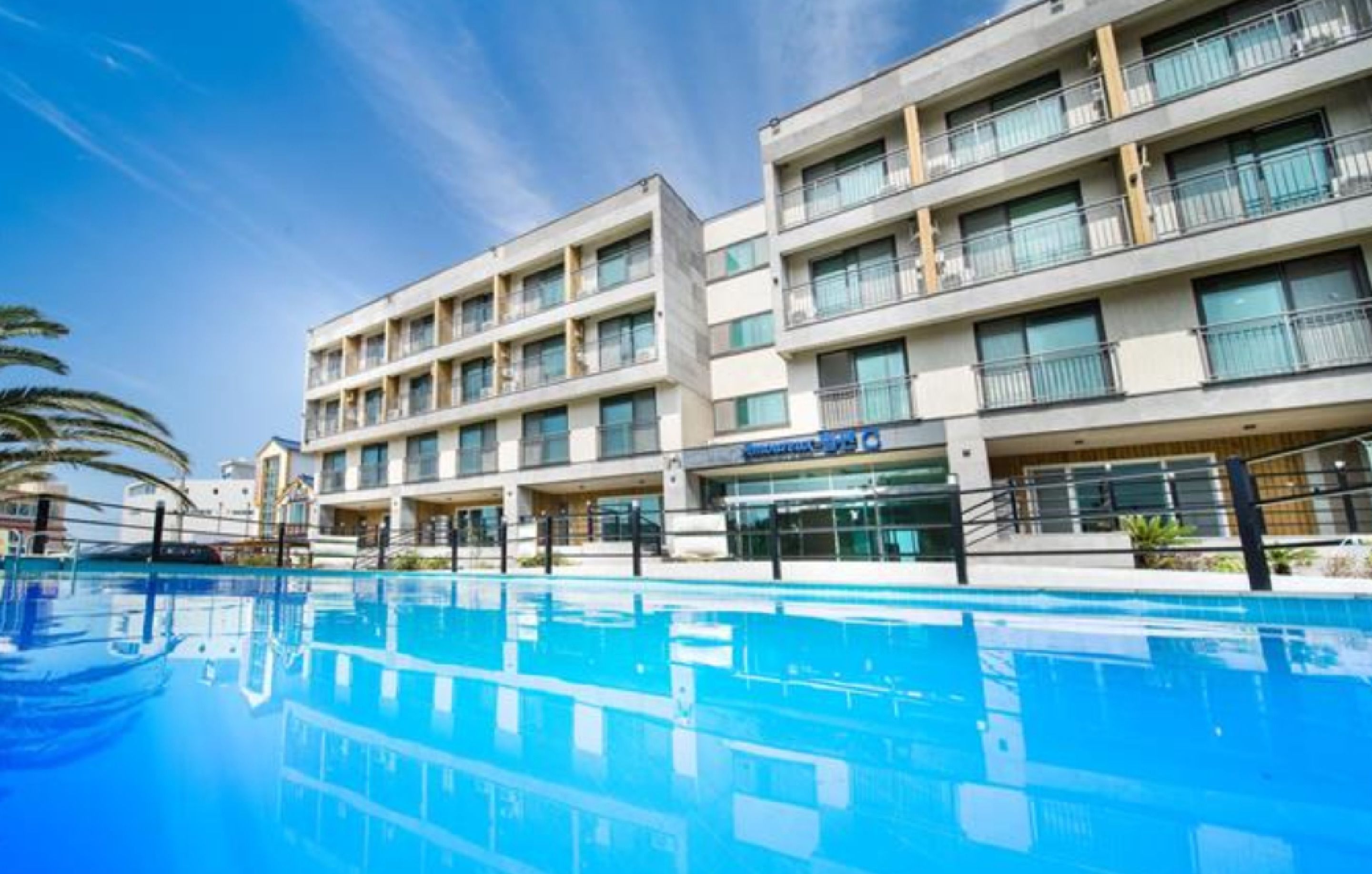 Um hotel moderno com piscina, várias varandas e um céu azul límpido.