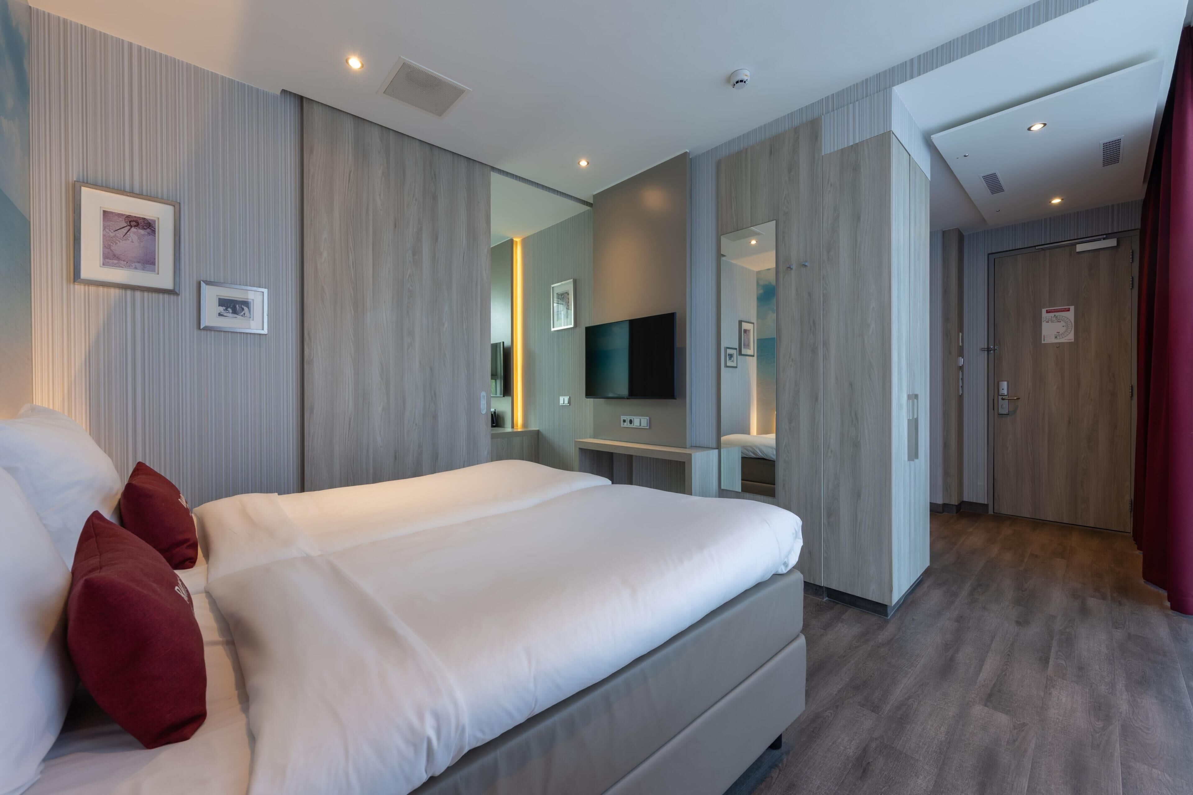 Quarto de hotel moderno com uma cama grande, uma TV de tela plana, uma escrivaninha e um espelho.