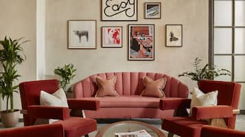 Uma sala de estar com um sofá vermelho, duas poltronas, uma mesa de centro e obras de arte emolduradas na parede.