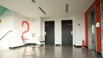 Um lobby moderno com uma escada, duas portas identificadas com os números 208 e 207, e um extintor de incêndio.