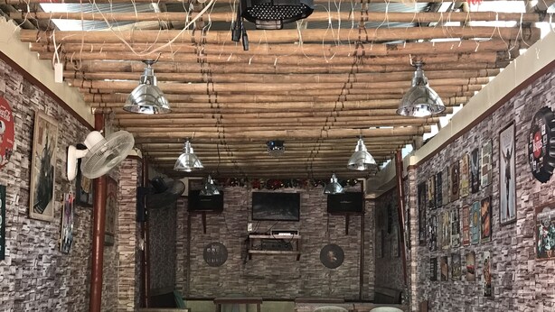 Um interior rústico com paredes de tijolo aparente, vigas de madeira no teto e várias mesas e cadeiras.