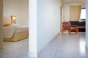 Quarto de hotel com cama, poltrona, sofá e janela com cortinas.