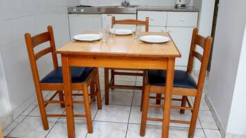 Uma mesa de jantar de madeira com quatro cadeiras, cada uma com uma almofada escura. A mesa está posta com pratos brancos, copos e uma faca.