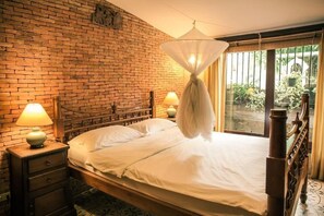 Quarto com parede de tijolos, cama com roupa branca, cabeceira de madeira e duas luminárias de cabeceira.