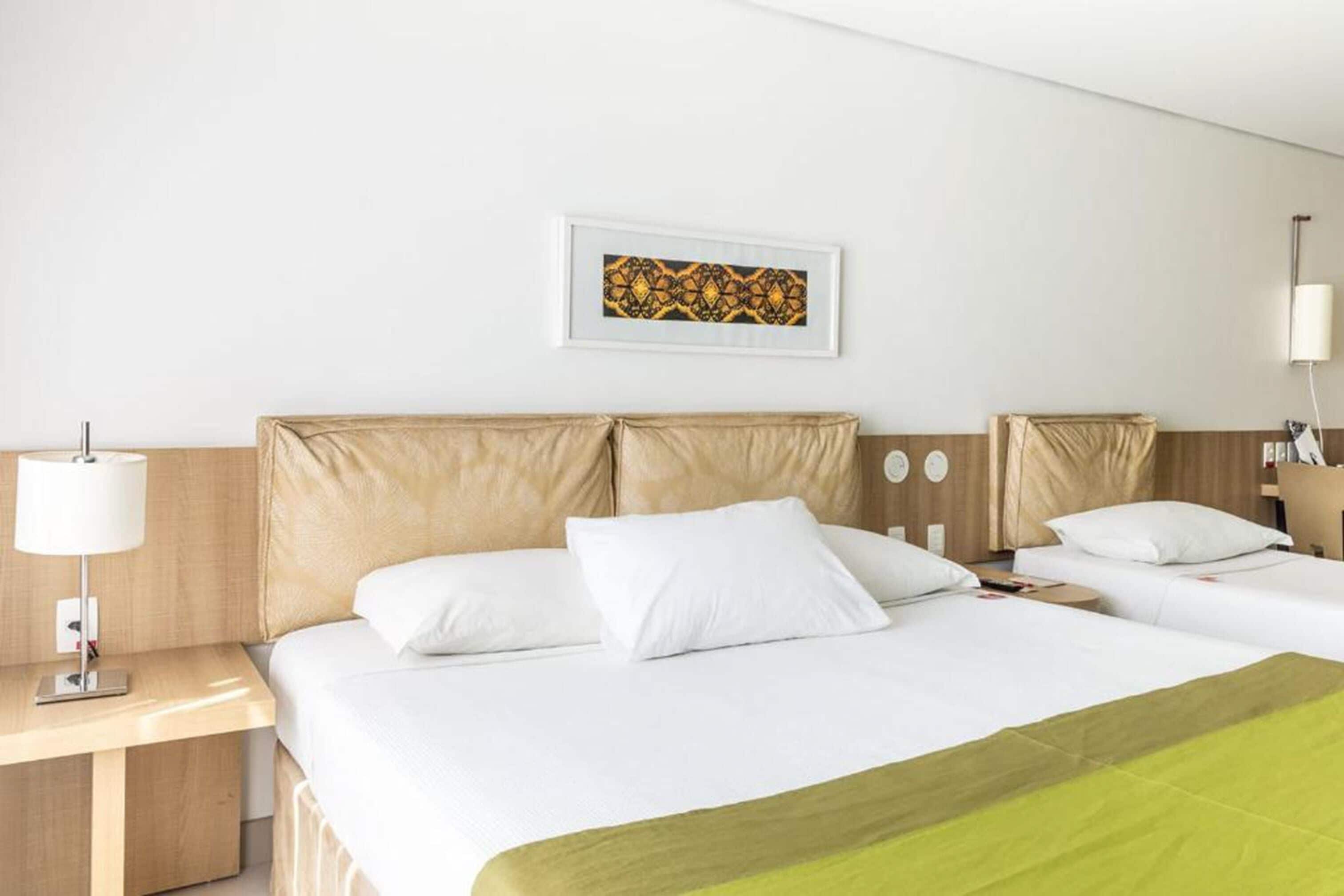 Quarto de hotel com cama, mesa de cabeceira, luminária e um quadro na parede.