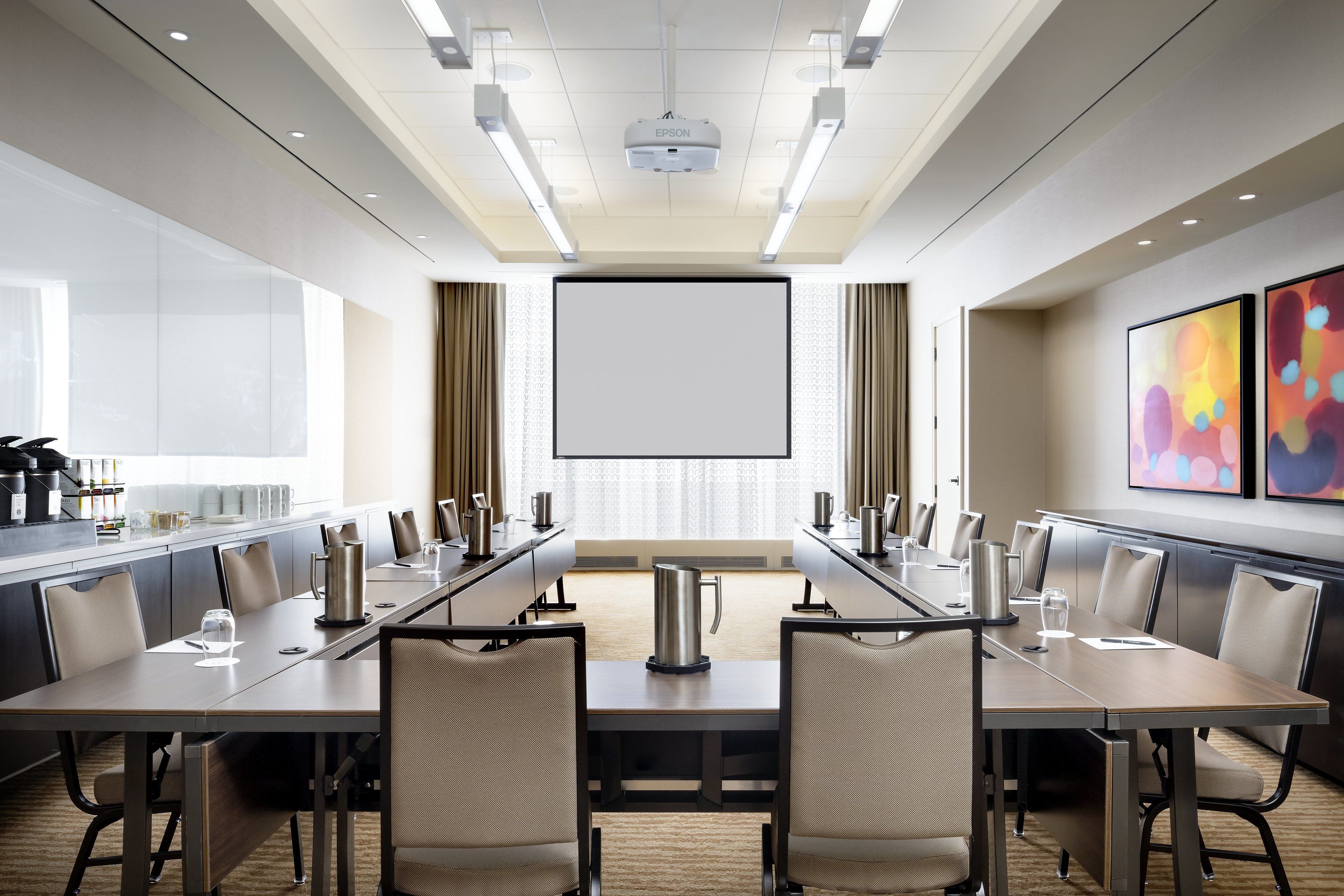Uma sala de conferências com uma mesa comprida, cadeiras, um projetor e uma tela grande.