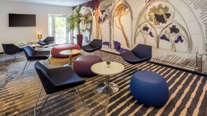 Uma área de estar moderna com assentos em preto e azul, uma mesa redonda e um mural com motivos florais e arquitetônicos.