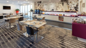 Uma área de refeições moderna em hotel, com mesas, cadeiras, um balcão de cozinha e um grande mural na parede.