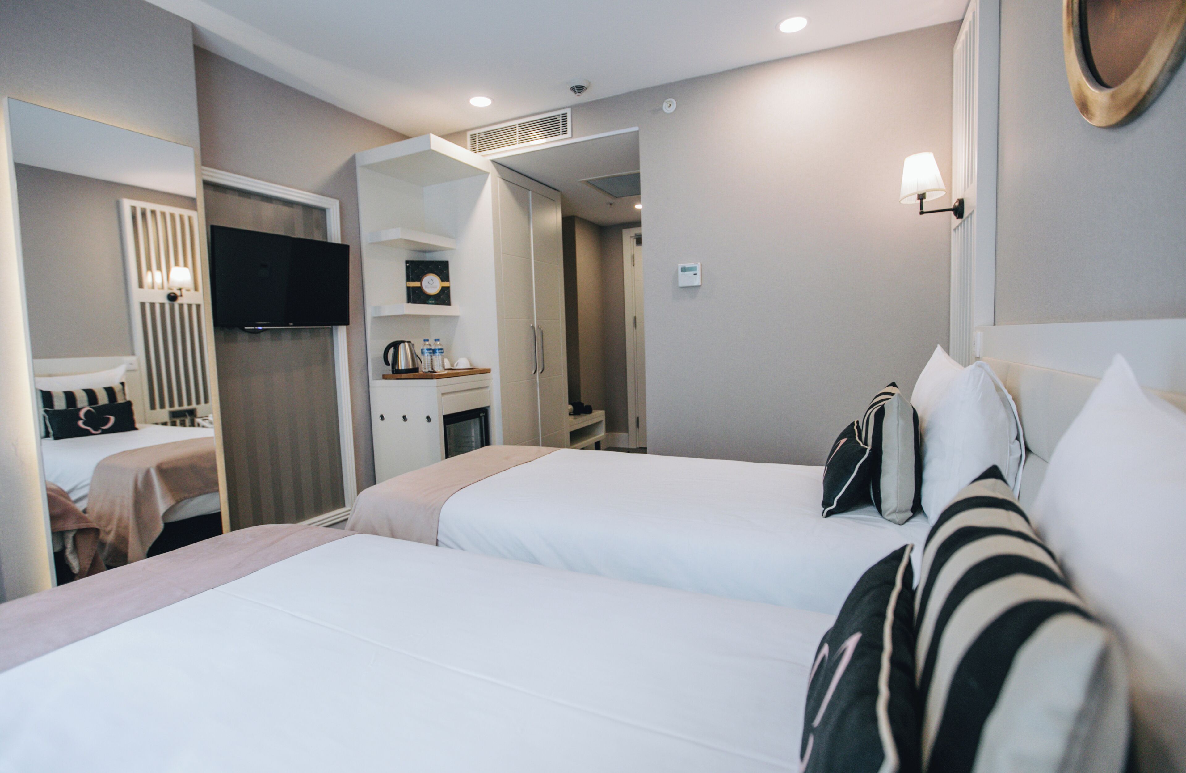 Quarto de hotel com duas camas, televisão, secretária com computador e casa de banho visível através de uma porta aberta.