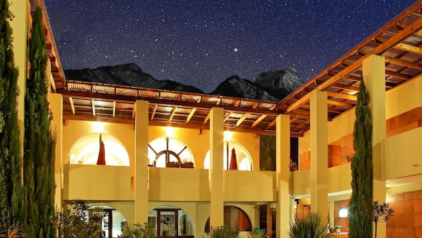 Um pátio com céu estrelado, área externa coberta com vigas de madeira e plantas em vasos.