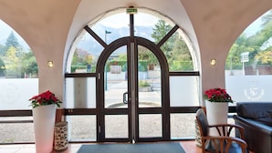 Entrada de hotel com uma grande porta em arco, balcão de recepção e área de estar com sofá e cadeiras.