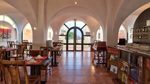 Uma ampla área de jantar com pé-direito alto e um espaço aberto central. Mesas montadas com cadeiras, e uma área de bar com estantes visíveis.