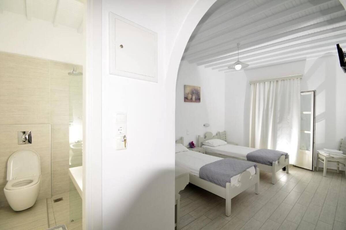 Quarto de hotel moderno com chuveiro, duas camas, uma mesinha e uma janela com cortinas.
