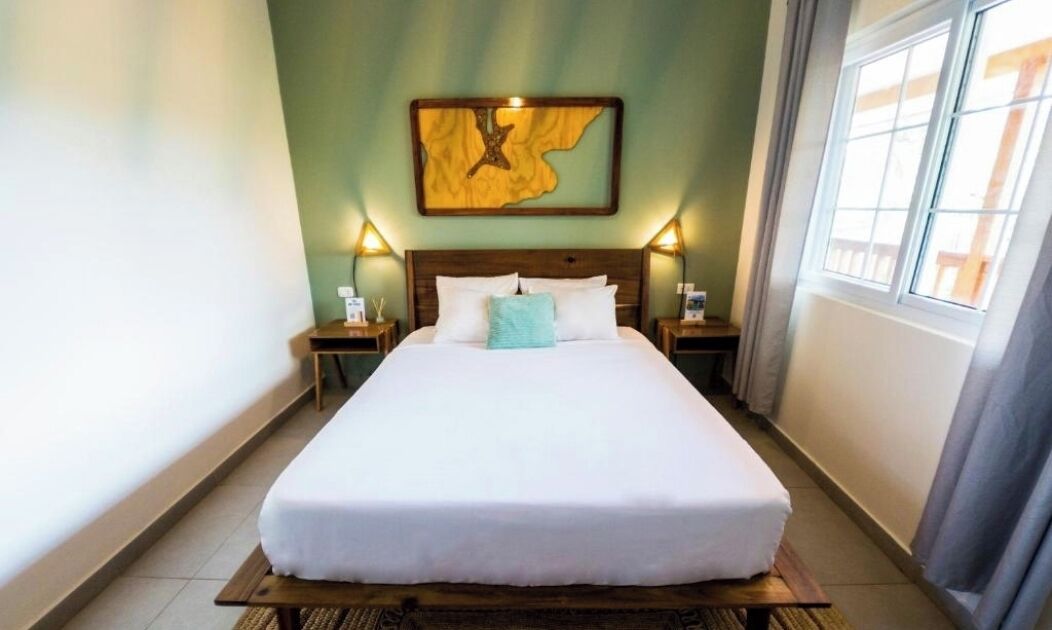 Uma cama bem arrumada com cabeceira de madeira, duas mesas de cabeceira com luminárias e uma obra de arte pendurada na parede.