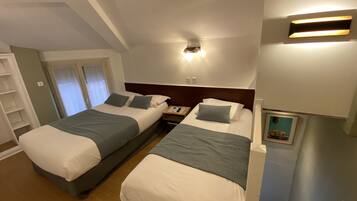 Quarto de hotel com duas camas, uma mesinha de cabeceira, uma luminária na parede e um quadro emoldurado.