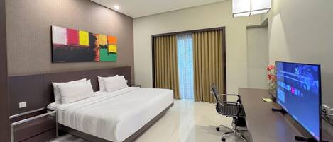 Quarto de hotel com uma cama grande, uma escrivaninha com computador, televisão e janela com cortinas.