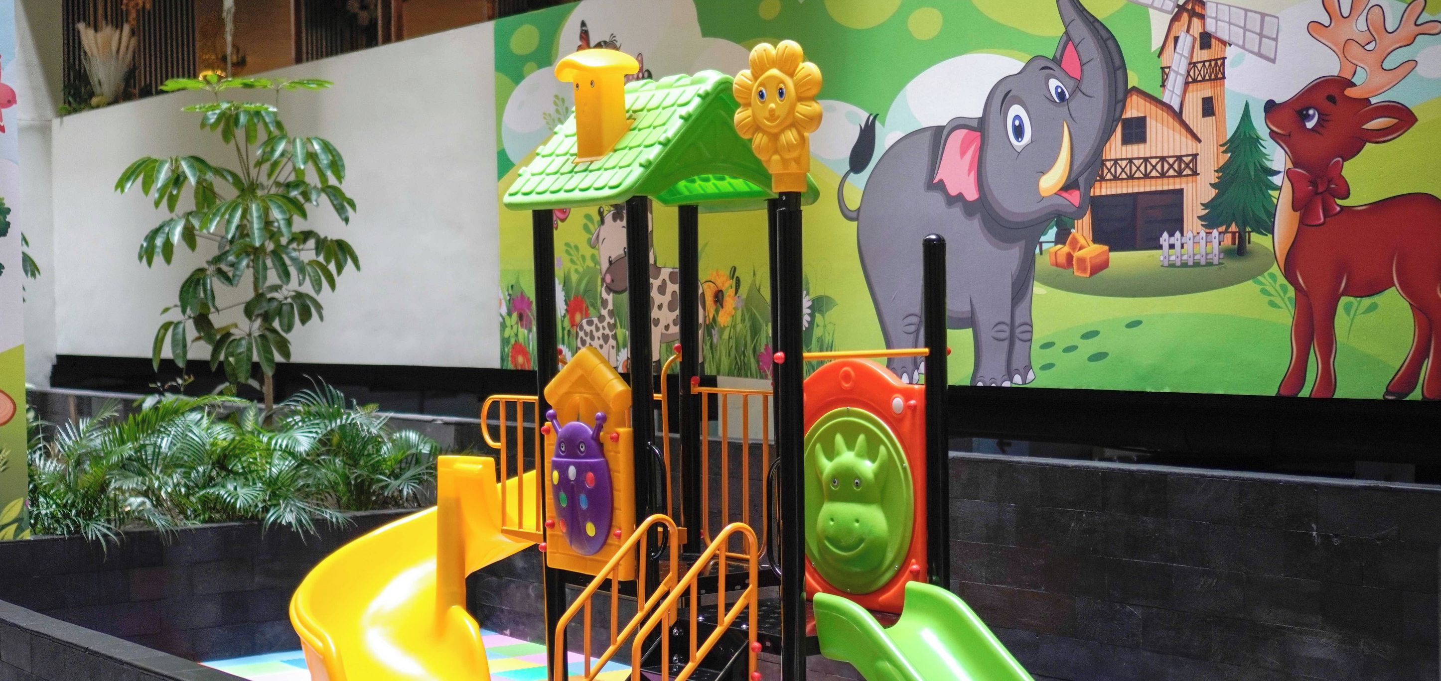 Espaço de recreação infantil com escorrega, estruturas de escalada e um mural ao fundo.